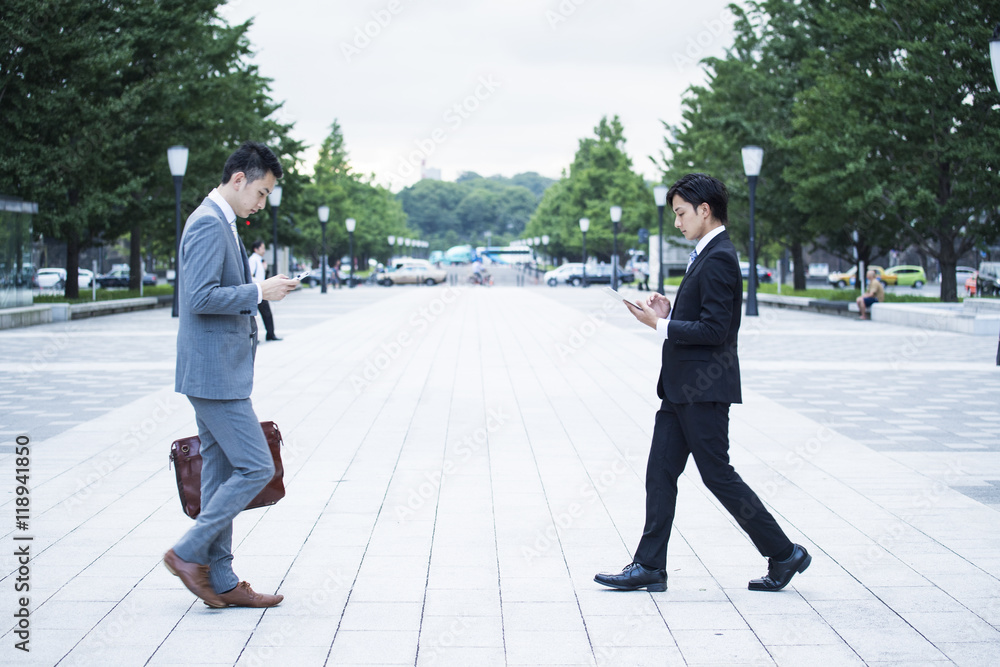 Businessman looking at mobile phone while walking Stock Photo | Adobe Stock