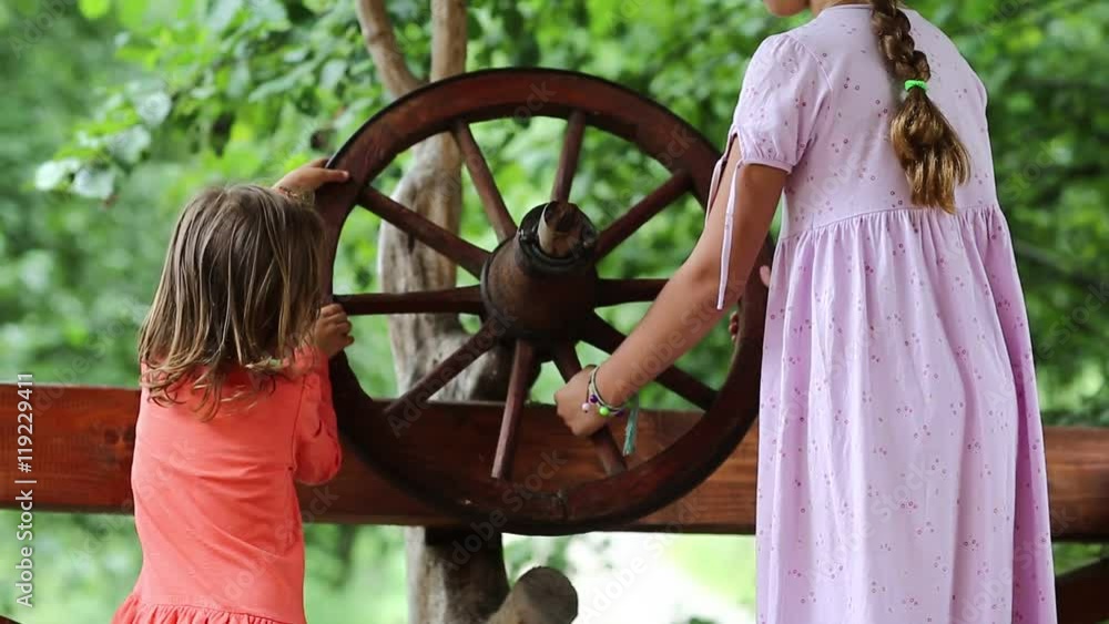 Two girls turn wooden wheel together. Sisters turn wooden wheel and ...