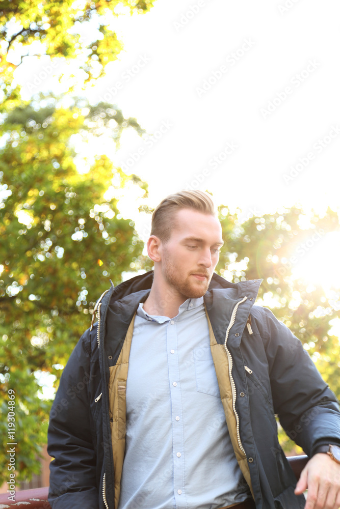 A sad man standing leaning back against a rail outside with the sun ...