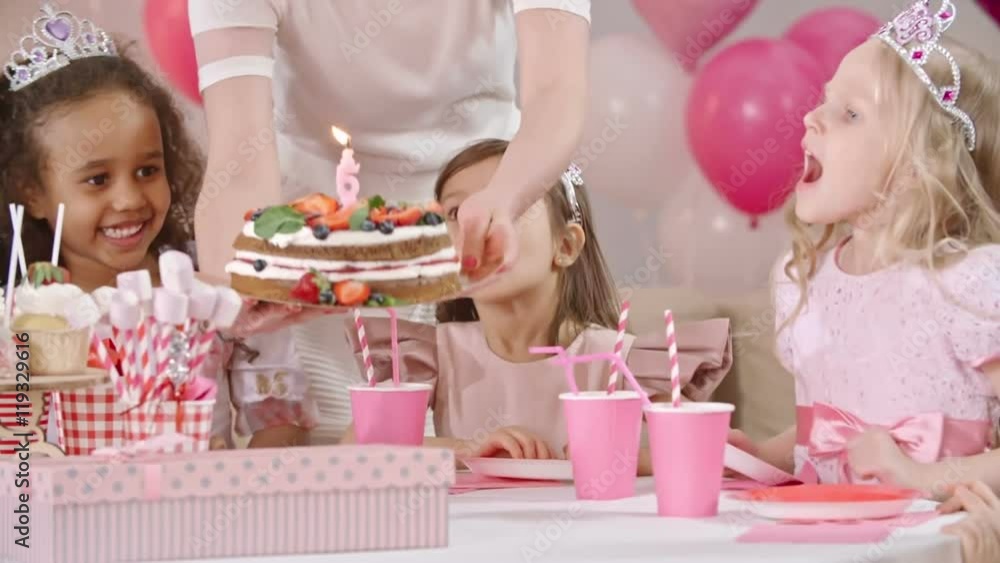 Woman putting birthday cake on table and little girls dressed like ...