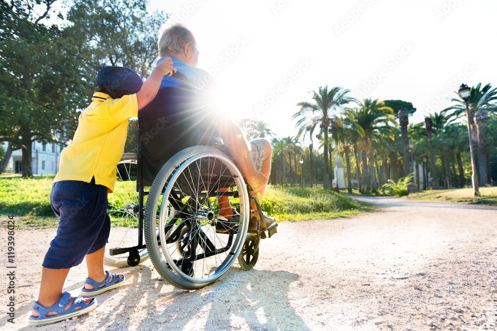 child pushing the wheelchair of grandfather, welfare and new generation ...