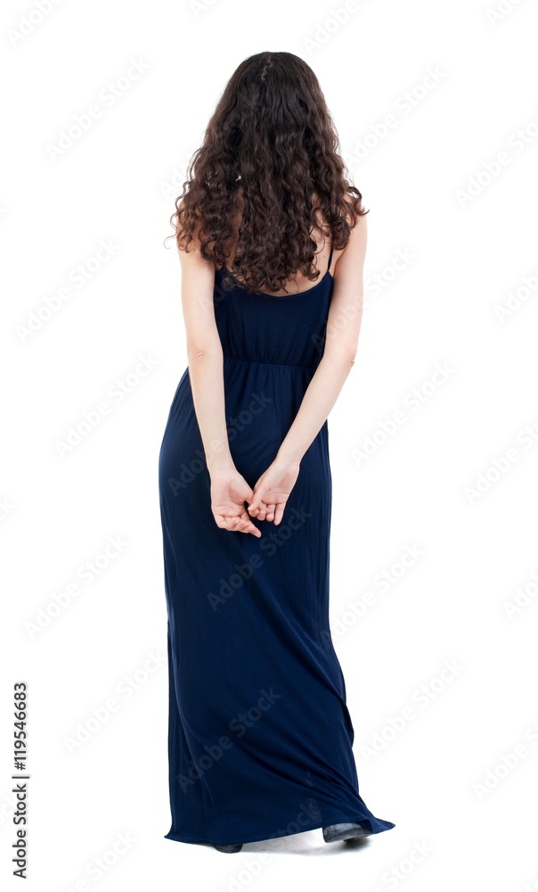 back view of standing young beautiful woman. dark curly girl in a blue ...