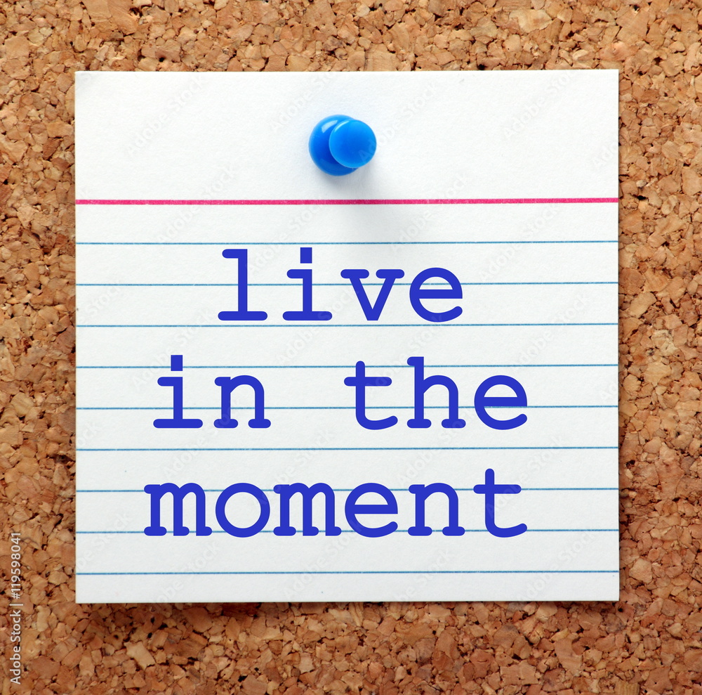 The words Live in the Moment printed on a note card pinned to a cork ...