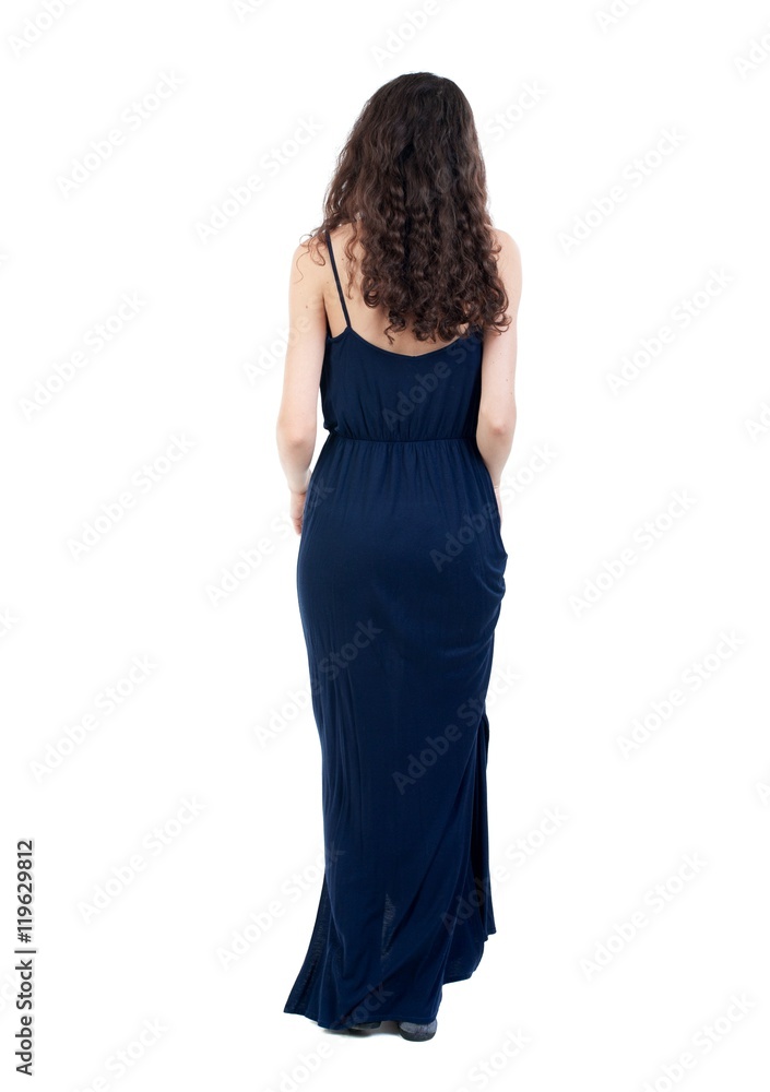 back view of standing young beautiful woman. dark curly girl in a blue ...