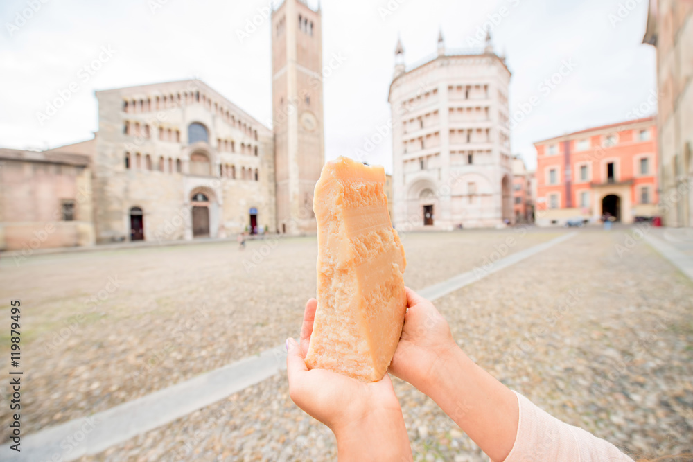Holding a piece of Parmesan cheese on the Parma main square background ...