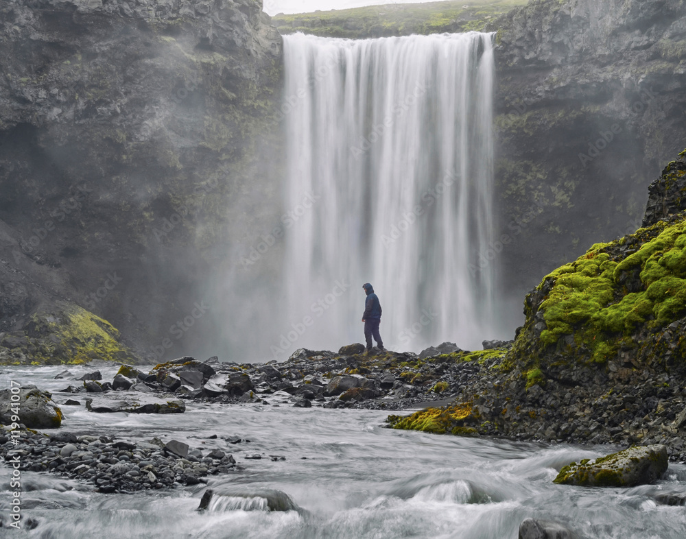 A man dressed in black standing at the base of a waterfall . Beautiful ...