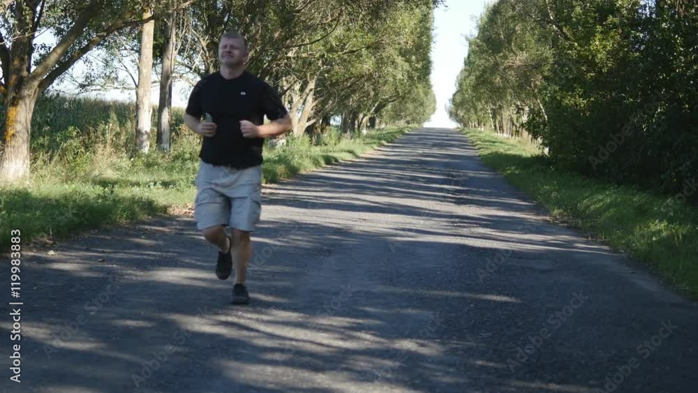 Adult man running outdoors in a forest path. Old man jogging outdoors ...