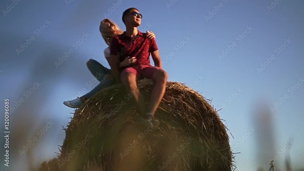 man and woman sitting on a haystack. man looking at the sunset and the ...