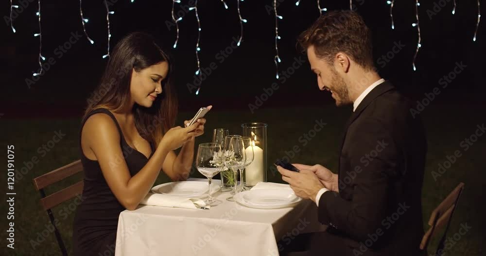 Young couple checking their mobiles during a romantic dinner in a ...