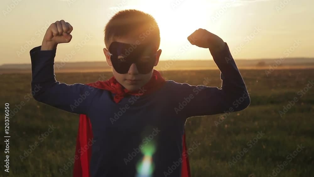 Boy dressed with a Superman cape running in a field, looking into the ...