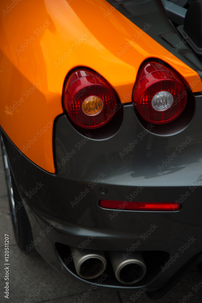 The rear lights and the exhaust pipe at the rear bumper of a sports car ...