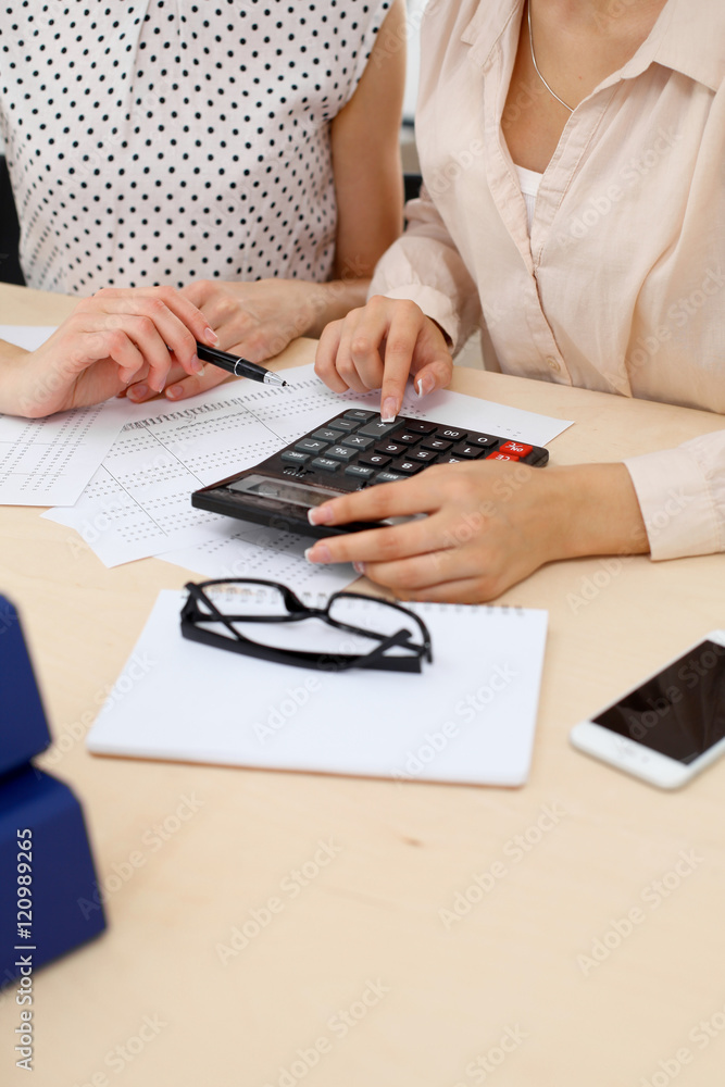 Two female accountants counting on calculator income for tax form ...