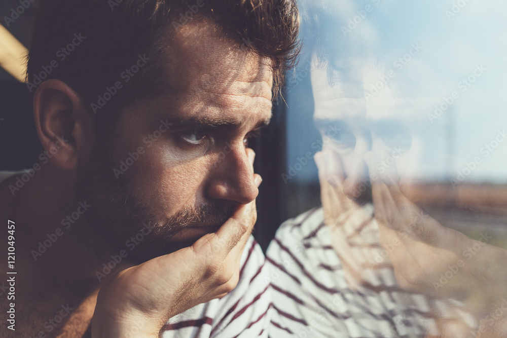 Sad young man looking through the window Stock Photo | Adobe Stock