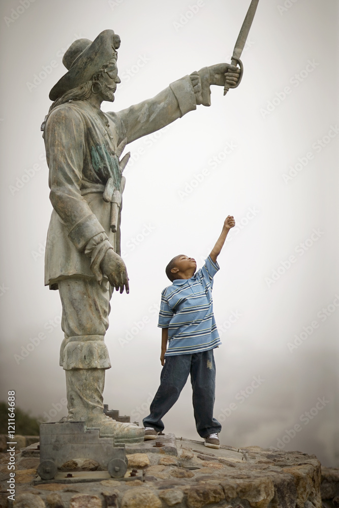 Young boy gesturing while standing next to a large statue. Stock Photo ...