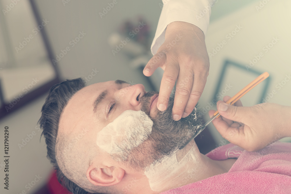 Client with foam on face during beard shaving in barber shop. Toned ...