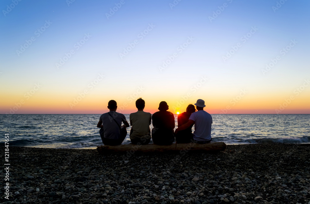 A group of people sitting on the beach and watching the sunset ...