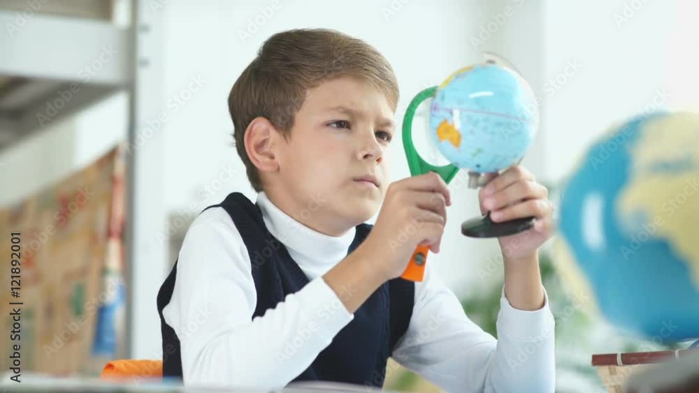 The boy looks at the globe using a magnifying glass. Globe on the desk ...