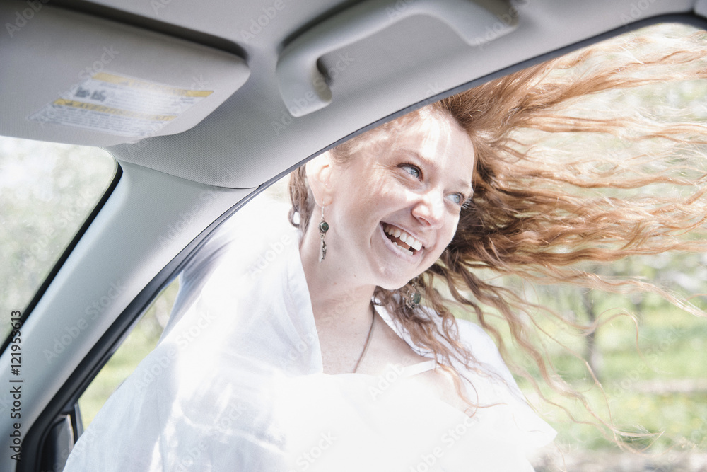 Woman on a road trip, leaning out of a car window, her long red hair ...