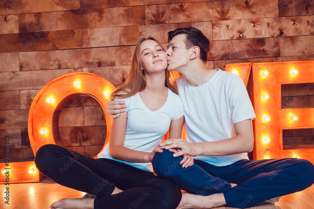 Young couple sitting at home on the floor and man kissing girl the ...