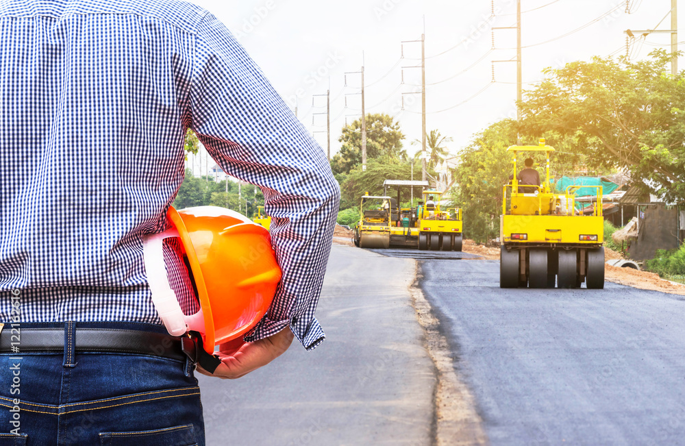 engineer holding safety helmet at road construction site with roller ...