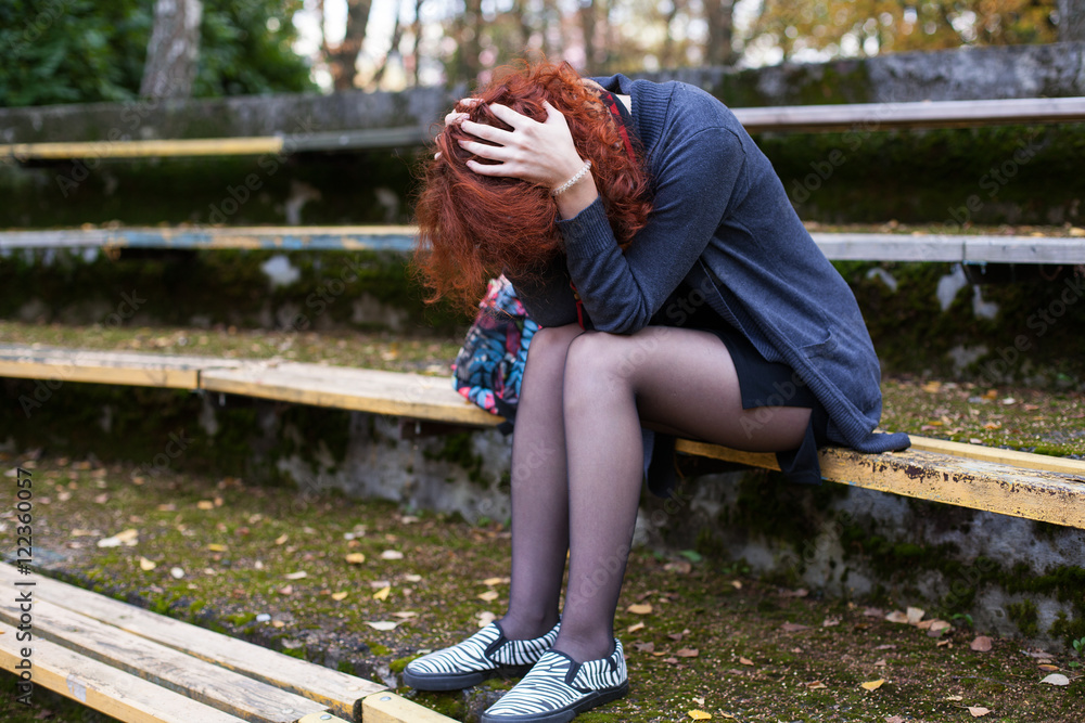Crying woman sitting on the bench, face is hidden by the hair, head ...