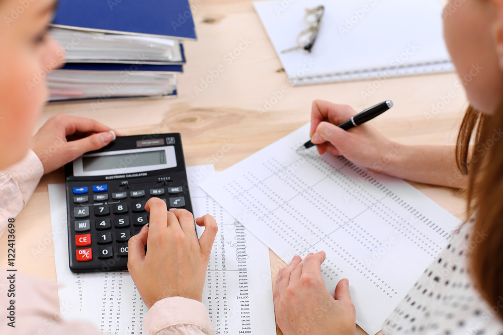 Two female accountants counting on calculator income for tax form ...