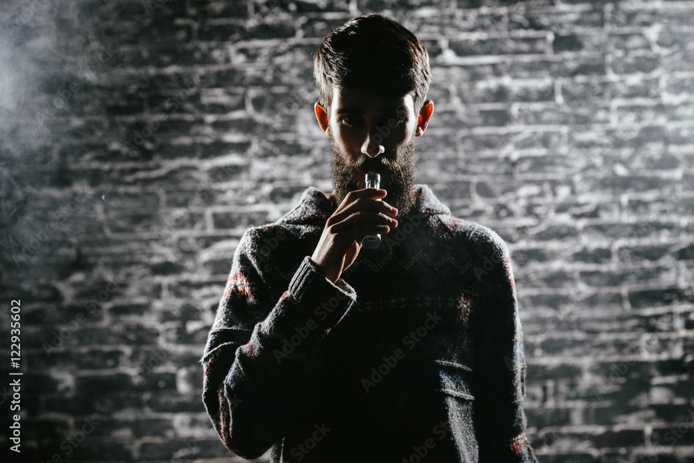 Young man with beard vaping an electronic cigarette. Vaper hipster ...