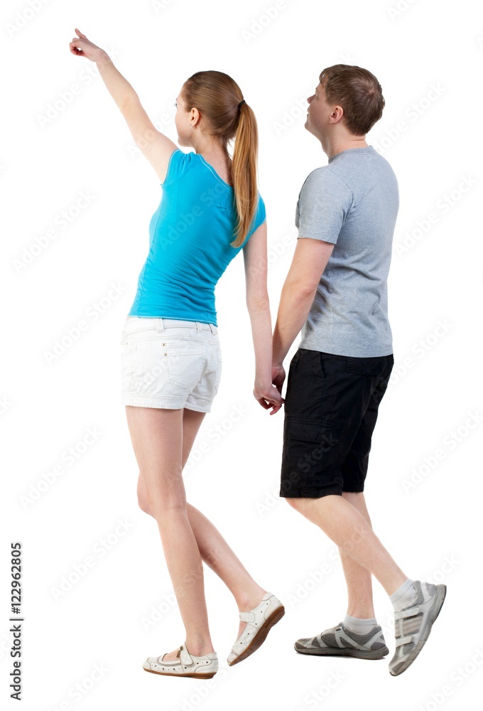 Back view of walking young couple (man and woman) pointing. curious ...