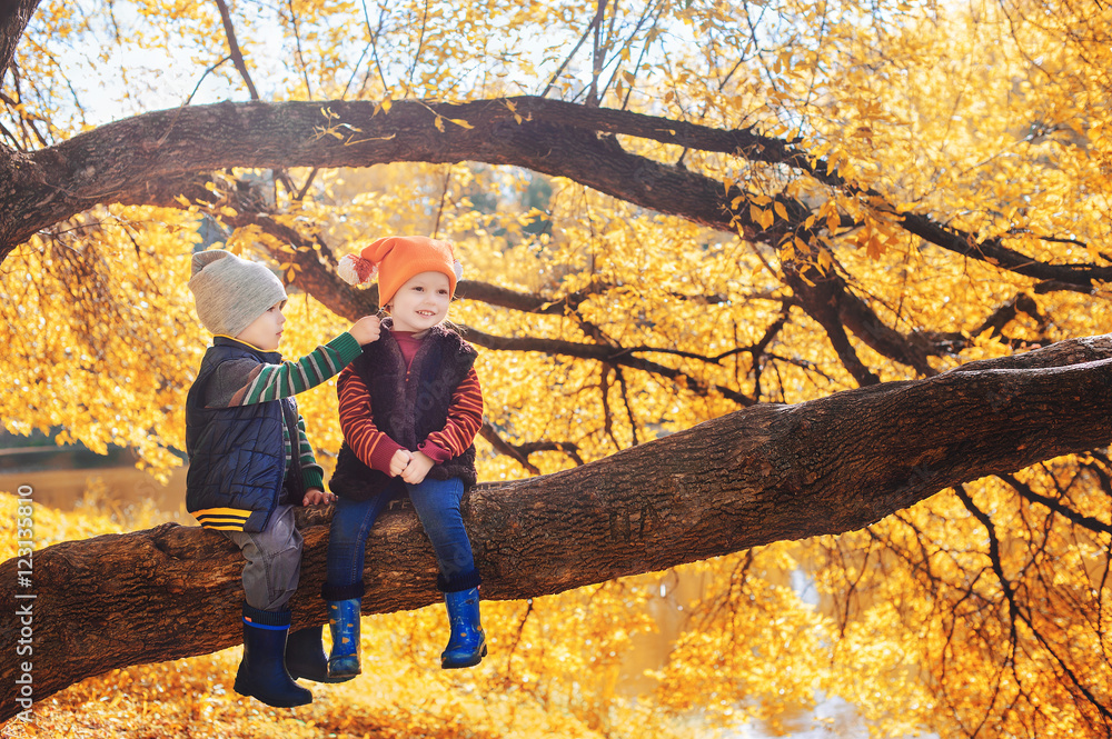 Little boy and girl sitting on a branch of tree in autumn forest Stock ...