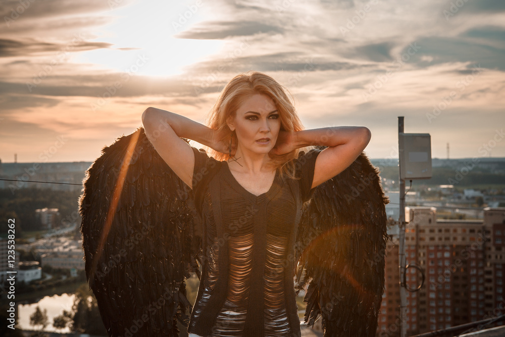 Portrait of a beautiful female angel demon on the roof in a black suit ...