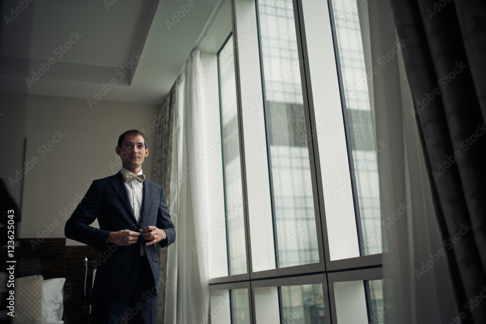 Man buttons up a tuxedo standing behind a big window in a hotel Stock ...