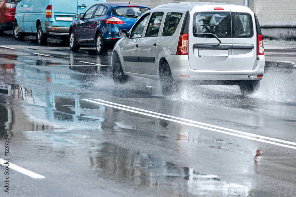 car traffic driving through rain puddles on the road during rush hour ...