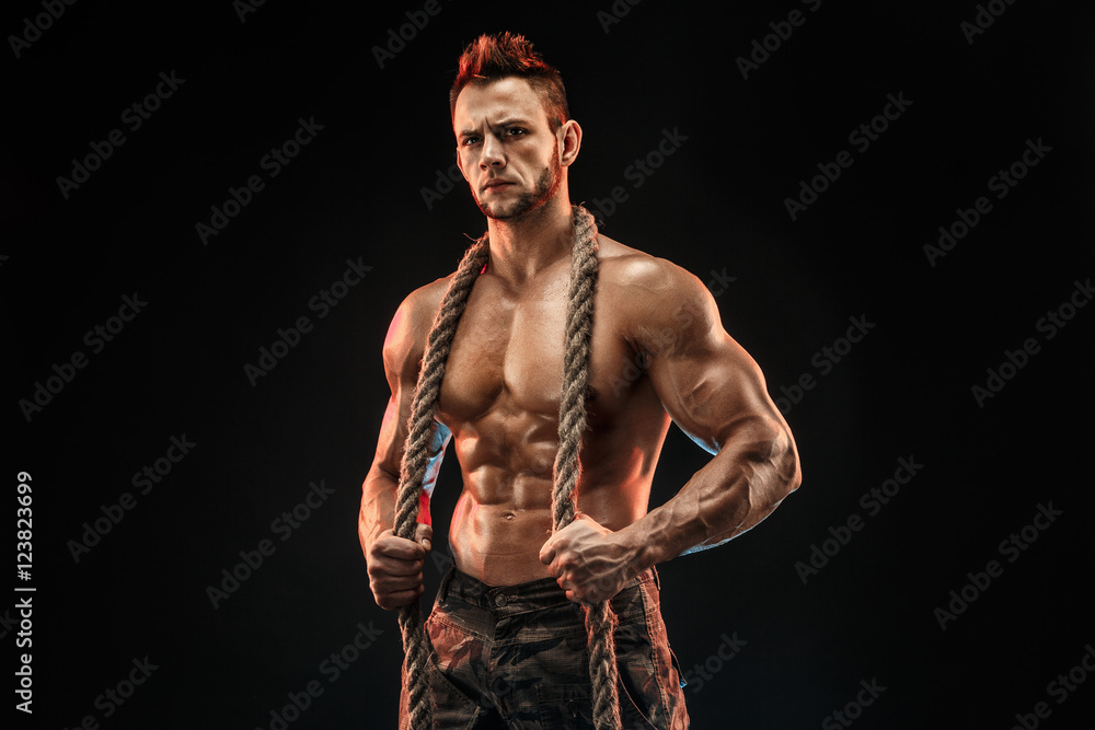 Muscular man holding rope and posing with serious face on the black ...