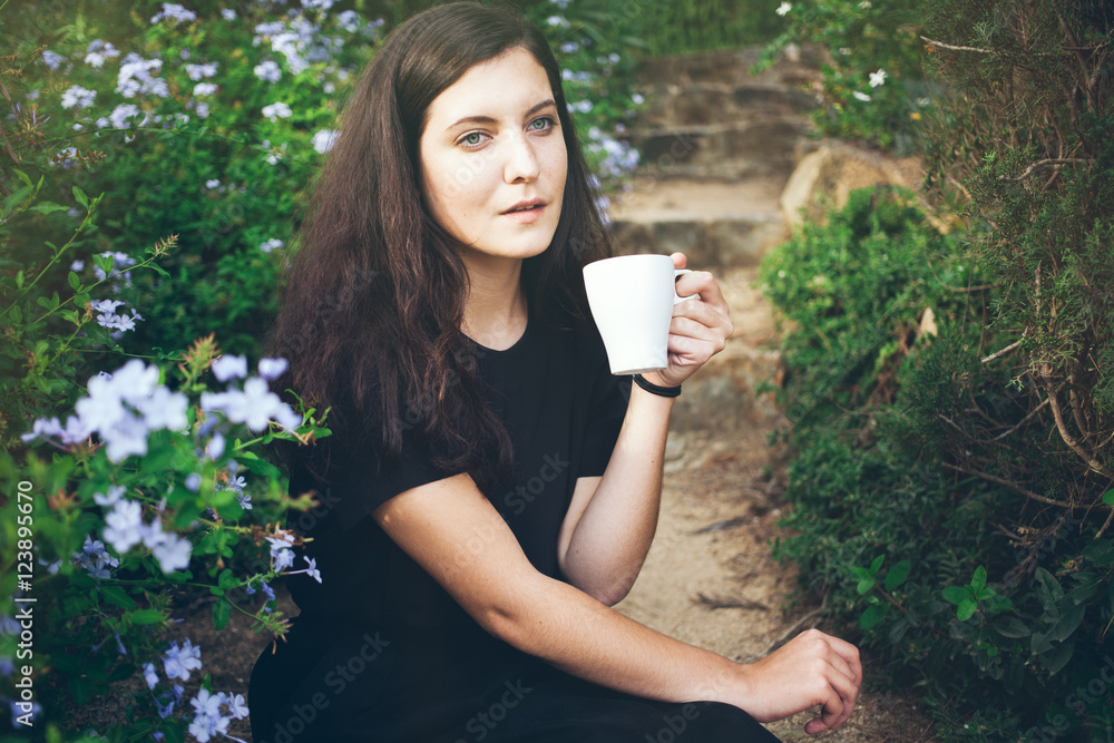 Young woman is drinking cup of tea in her garden, smelling fresh ...