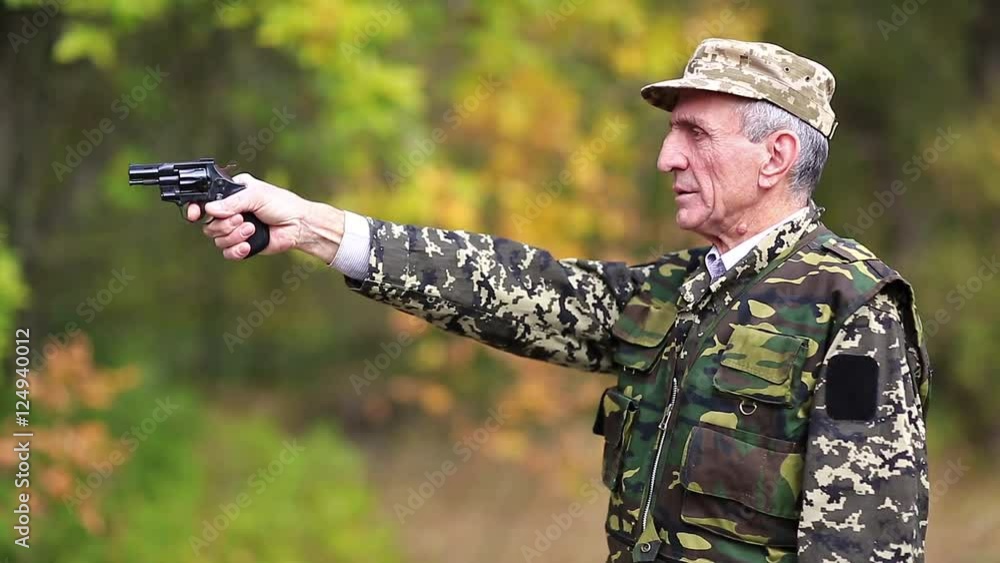 Elderly person in military uniform shoots a revolver. Retired officer ...