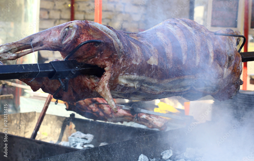 Carcass of a whole pigs meat roasting on a spit over hot coals at an ...