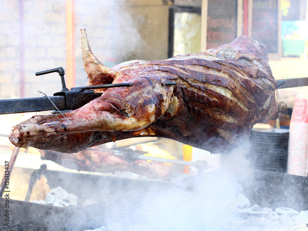 Carcass of a whole pig meat roasting on a spit over hot coals at an ...