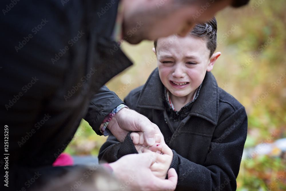Small boy crying in pain injuring his hand. Father provides first aid ...