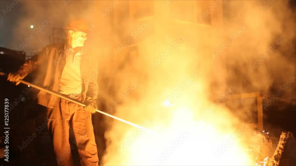 Hard work in the foundry, worker watching and controlling iron smelting ...