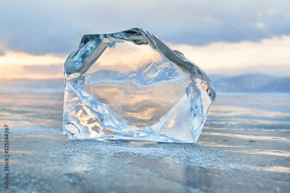 Transparent ice block at frozen surface with reflection and sunset sky ...
