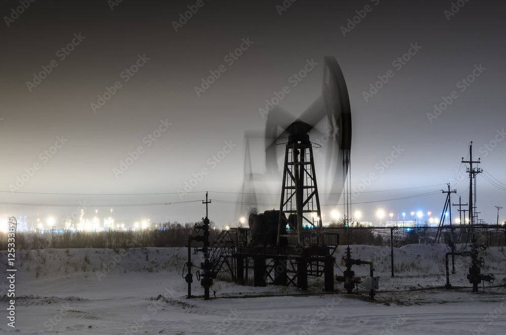 Working oil pump at night time. Oilfield during winter. Refinery lights ...
