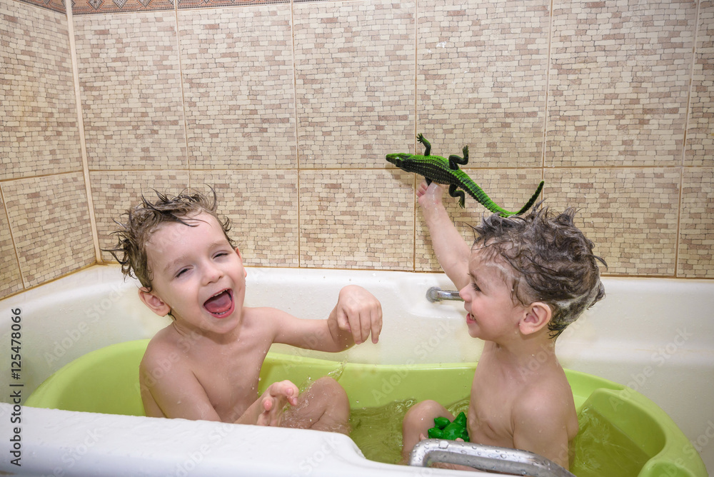 Two little twins children playing together with water by taking bath ...