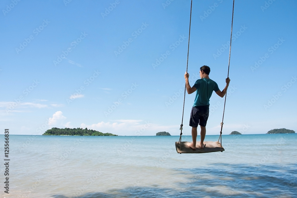 young man swinging on rope swing above water on idyllic paradise beach ...