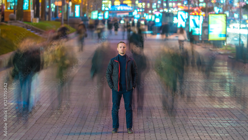 The serious man stand in the ghost-like crowd stream. Evening - night ...