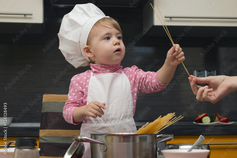 little cute girl in chef suit in the kitchen helping her mother cook ...