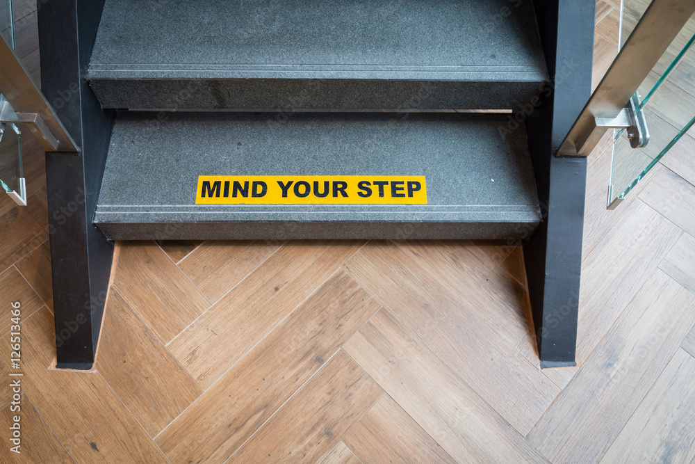 Yellow and black warning sign on stairs stating "Watch your Step Stock ...