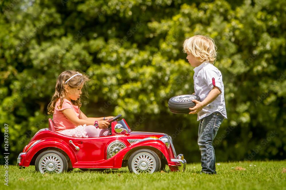 young happy children - boy and girl - driving a toy car outdoors Stock ...