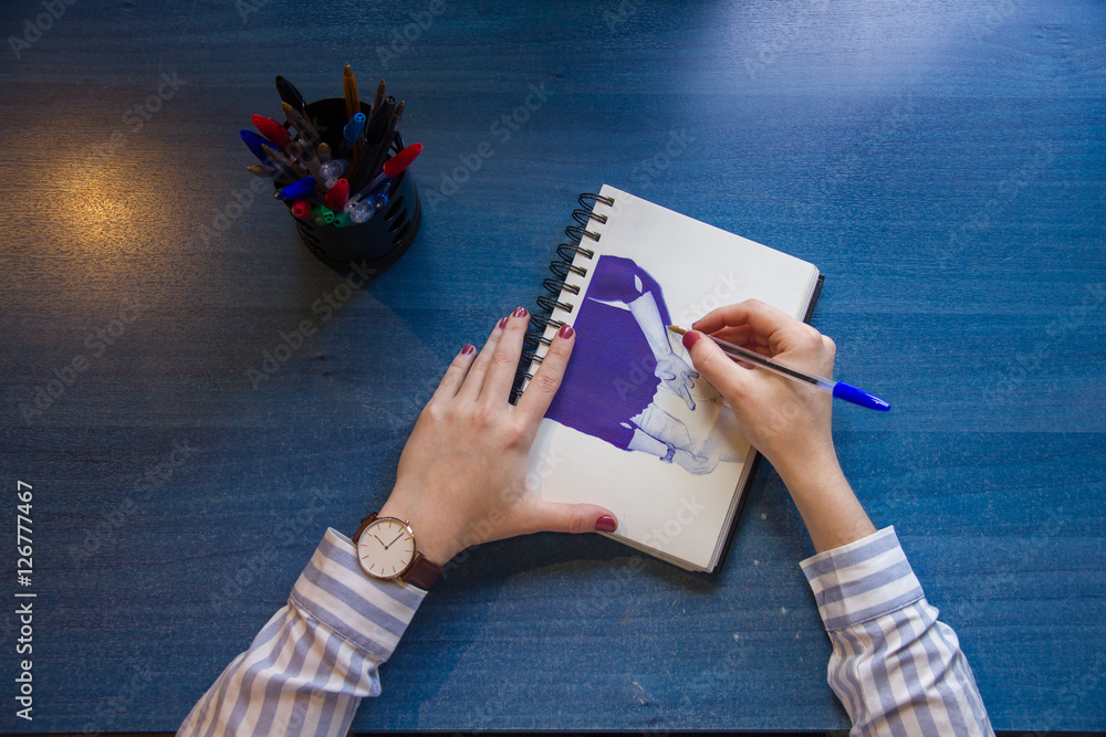 Girl drawing with blue pen a person in her drawing notebook on a blue ...