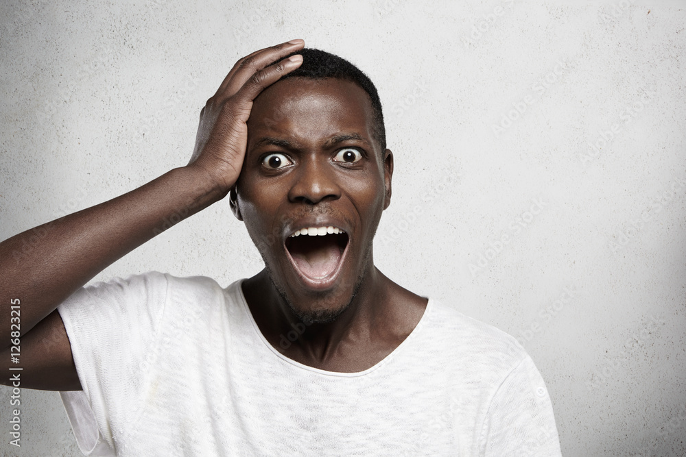 Headshot of terrified young African employee in white t-shirt holding ...