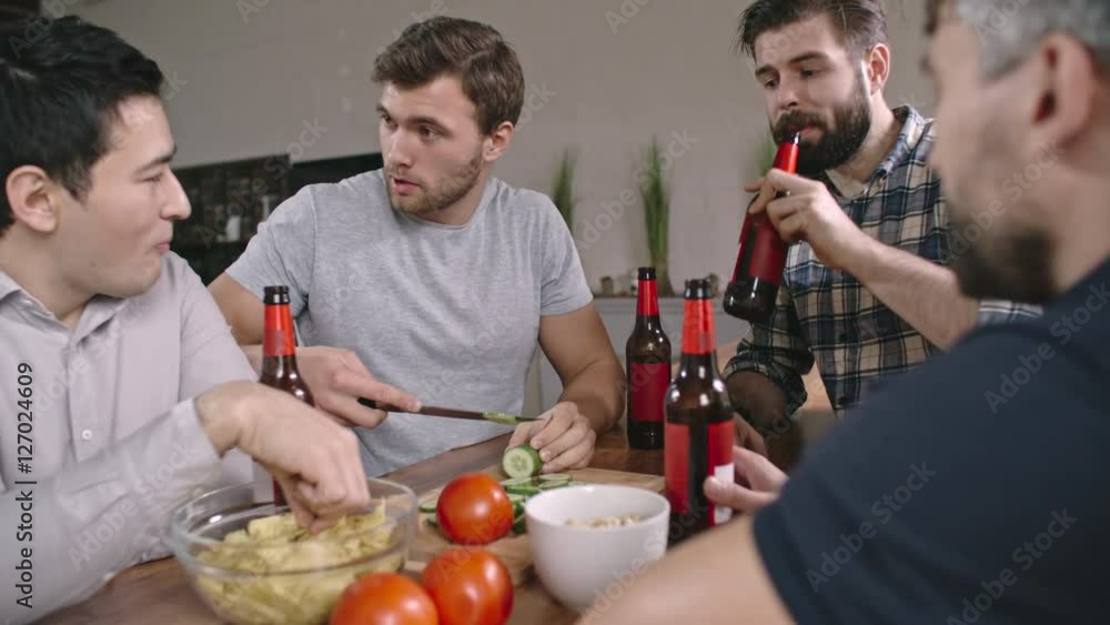 Man sitting behind table cutting vegetables and chatting with friends ...